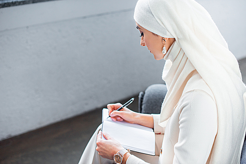 유토이미지 | high angle view of young muslim woman writing in notebook at home
