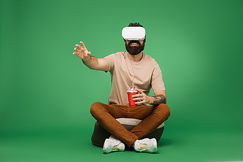 bearded man with paper glass of soda using Virtual reality headset ...