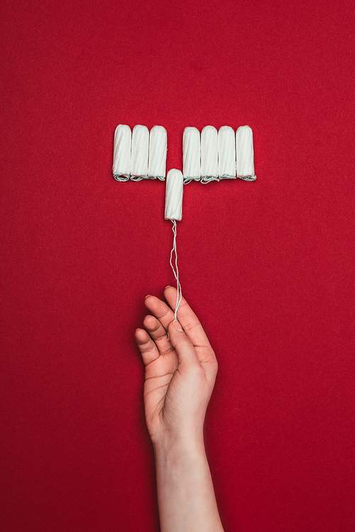 유토이미지 | cropped shot of woman holding tampon in hand isolated on red
