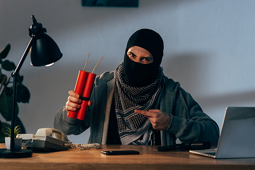 Angry terrorist in mask sitting at table and pointing with finger at ...