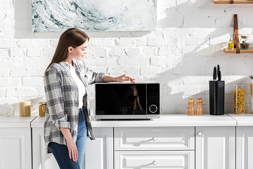 유토이미지 | smiling woman in shirt looking at microwave in kitchen