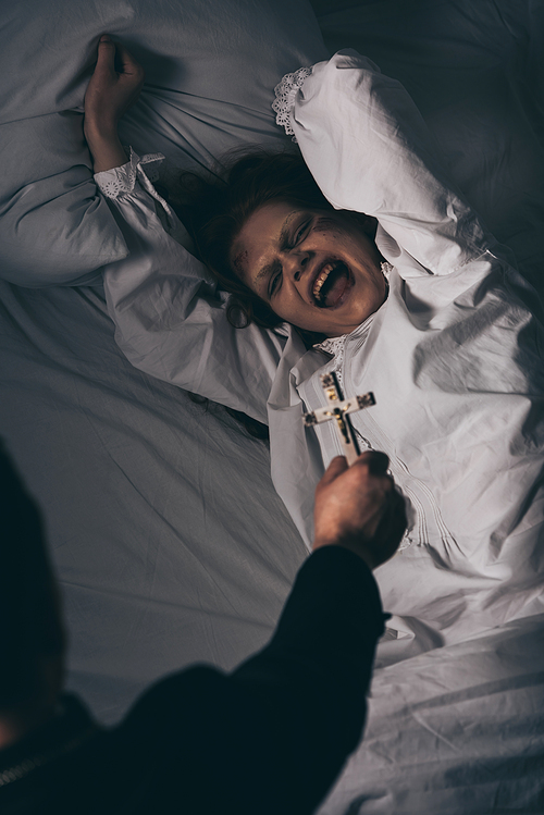 유토이미지 | exorcist holding cross over creepy screaming demon in bed