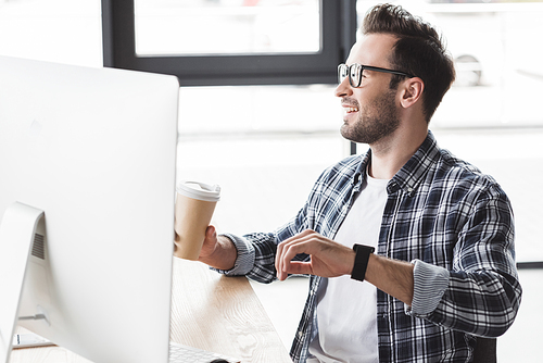 유토이미지 | handsome smiling young programmer in eyeglasses holding paper cup while working with ...