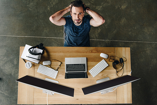 handsome young man with hands behind head while sitting at workplace ...