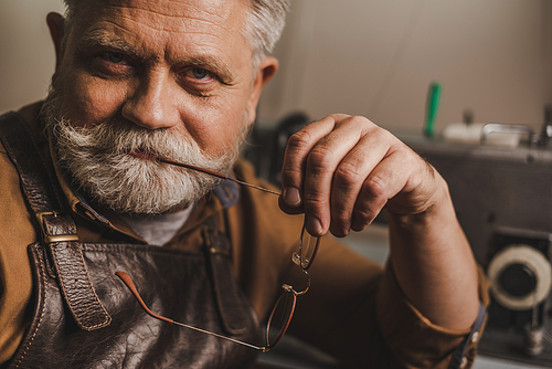 유토이미지 | positive, senior shoemaker smiling at camera while holding glasses