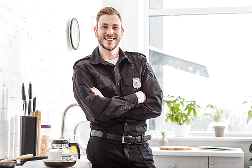 smiling police officer with crossed arms standing next to kitchen table ...