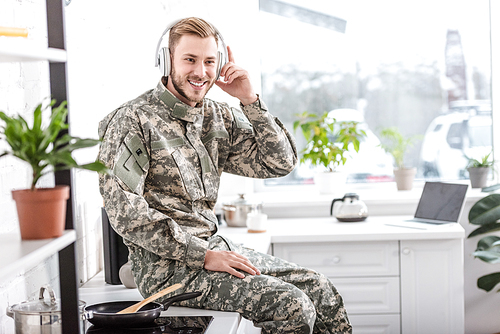 handsome soldier in headphones listening music and sitting on kitchen ...