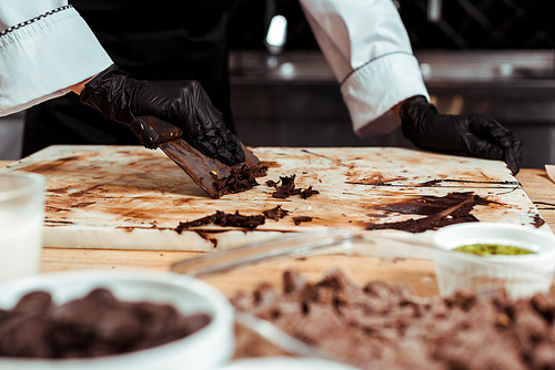 cropped view of chocolatier in black latex gloves scraping dark ...
