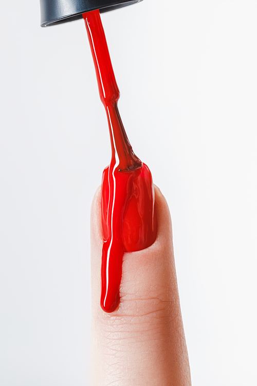 partial view of woman applying dripping red nail polish on fingernail ...