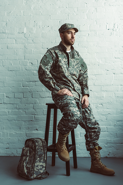 pensive soldier in military uniform sitting on chair against white ...