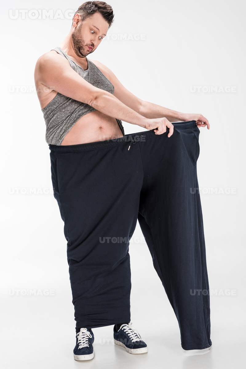 surprised overweight man holding oversize pants after weight loss on ...