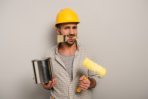 frustrated repairman in hardhat holding paint roller, brush and can ...
