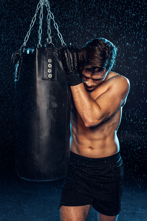 exhausted boxer in black briefs holding punching bag and looking down ...