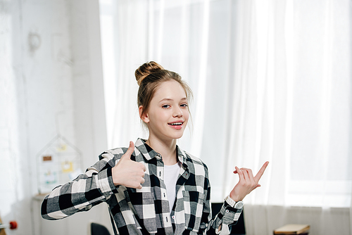Smiling teenager in checkered shirt showing thumbs up at home | 유토이미지 ...