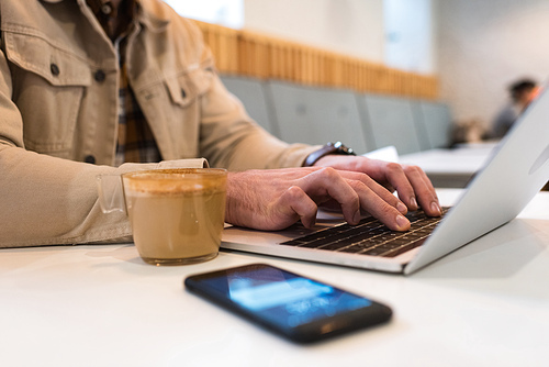 Cropped view of freelancer with cup of coffee typing on laptop keyboard ...