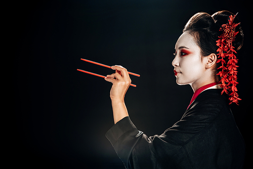 side view of beautiful geisha in black kimono with red flowers in hair ...