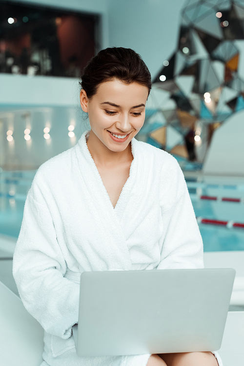 유토이미지 | attractive and smiling woman in white bathrobe using laptop in spa