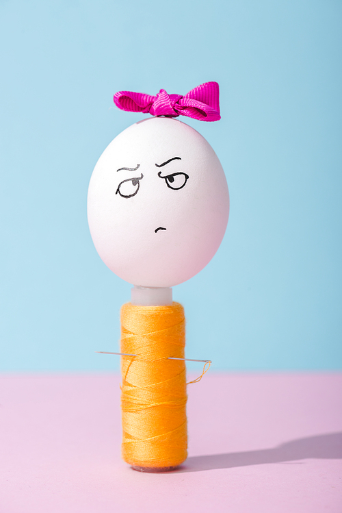 유토이미지 | egg with bow and angry face expression on thread coil on blue ...