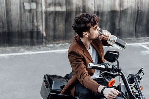 man in brown jacket drinking alcohol from bottle while sitting on ...