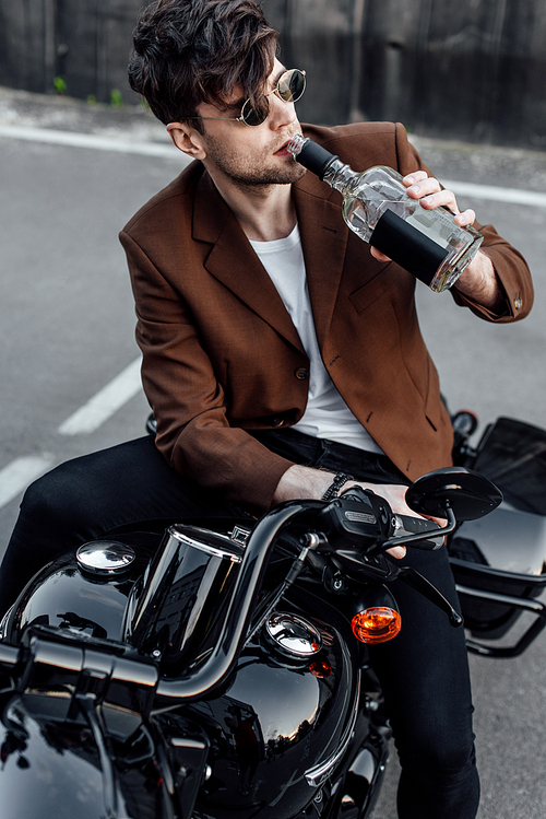 handsome man in sunglasses and brown jacket drinking alcohol from ...