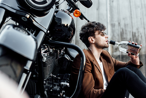 selective focus of man drinking alcohol while leaning on motorcycle and ...