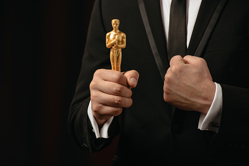partial view of man in suit with clenched fist holding oscar award ...