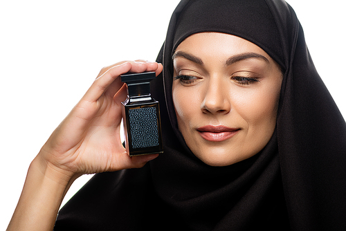 young Muslim woman in hijab looking at bottle of perfume isolated on ...