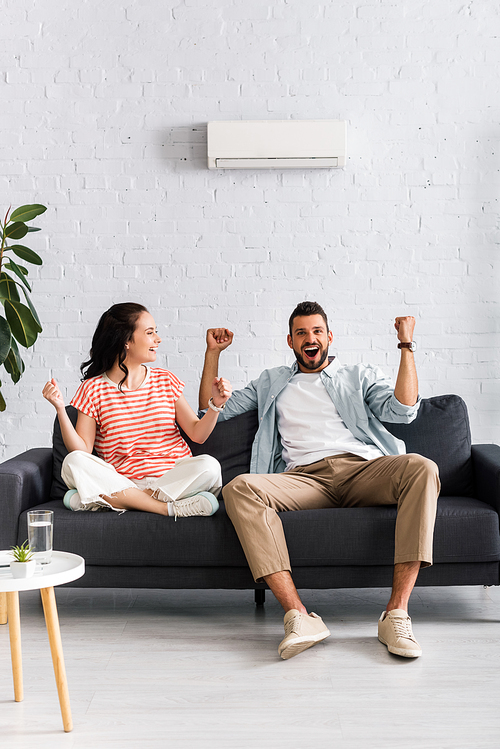 Smiling couple showing yes gesture while sitting under air conditioner ...