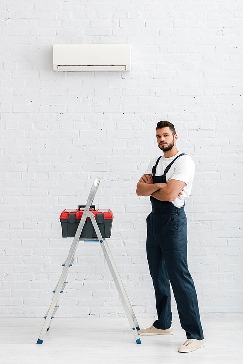 Handsome handyman near toolbox on ladder and air conditioner on white ...