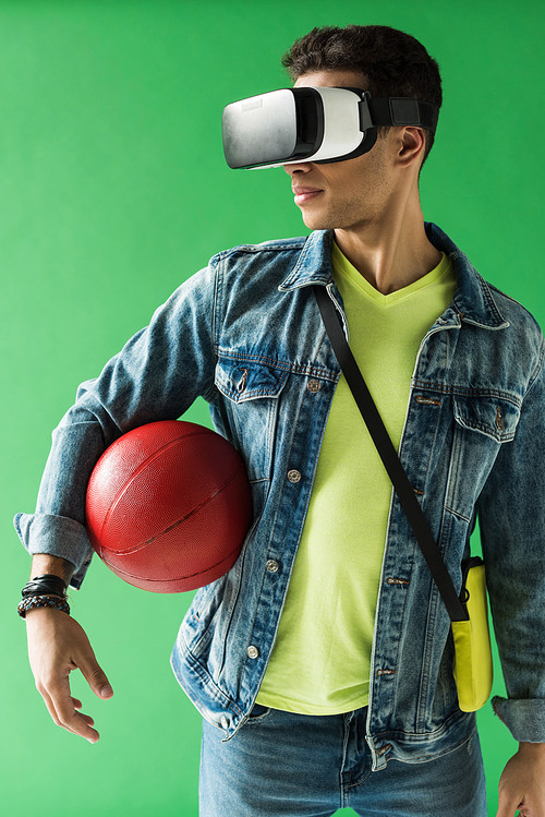 mixed race man in virtual reality headset holding basketball on green ...