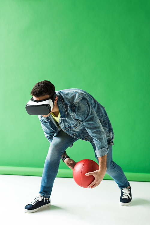 mixed race man in virtual reality headset holding basketball on green ...