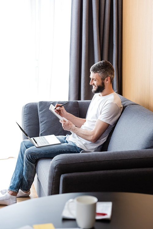 Selective focus of smiling teleworker working with laptop and notebook ...