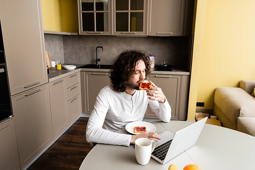유토이미지 | handsome freelancer eating toast while using laptop near coffee ...