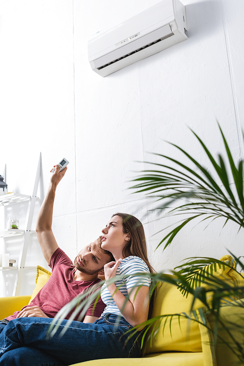 sad couple with remote controller suffering from heat at home with ...