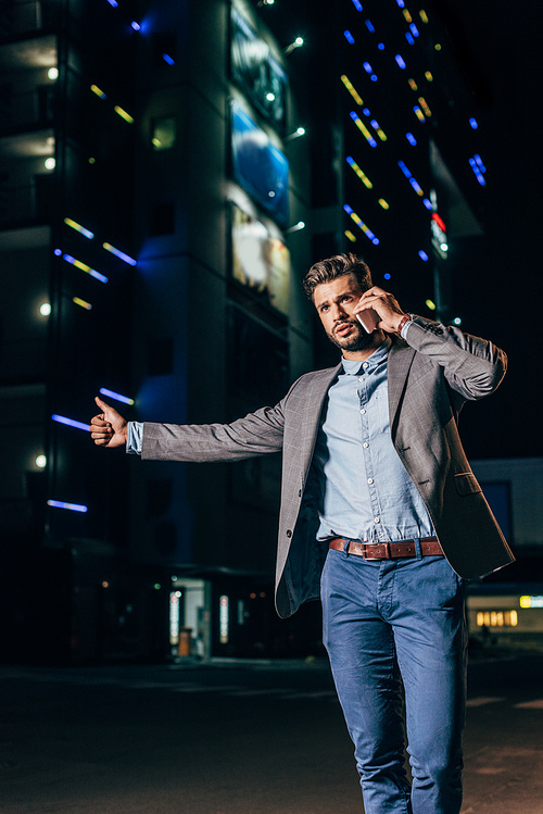 handsome businessman in formal wear talking on smartphone and thumbing ...