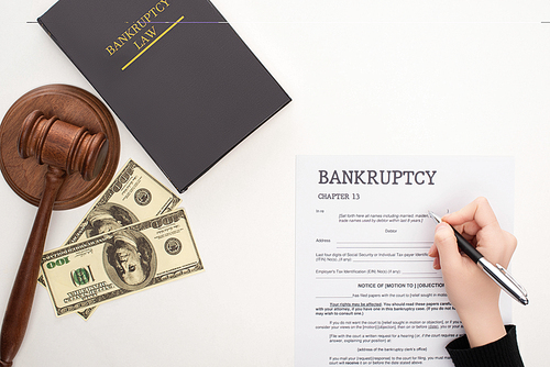 cropped view of woman filling in bankruptcy form with pen near money ...