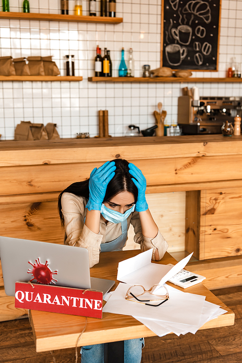 Stressed cafe owner in medical mask looking at papers near calculator ...