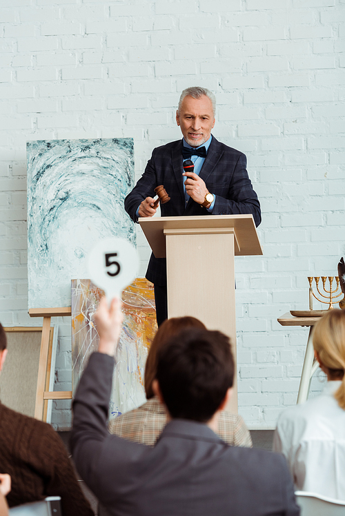 selective focus of smiling auctioneer talking with microphone and ...