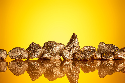 pile of gold shiny stones in row with reflection on yellow background ...