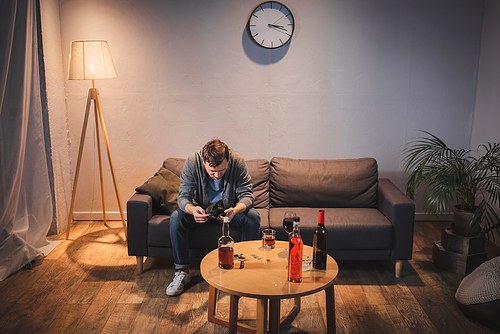 alcohol-addicted man holding empty wallet near table with bottles at ...