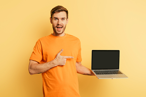 excited young man pointing with finger at laptop with blank screen on yellow background | 유토이미지 ...