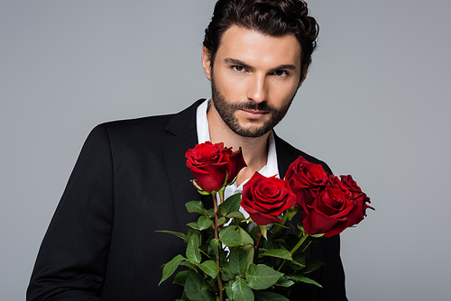 bearded young man in suit holding bouquet of red roses while isolated ...