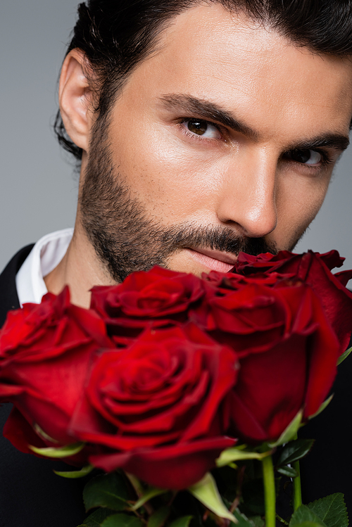 close up of bearded man holding bouquet of red roses isolated on grey ...