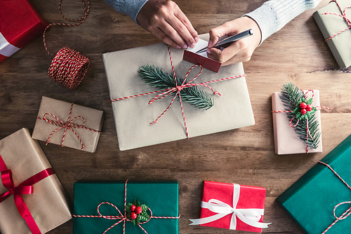 Woman writing Christmas greeting card on gift box at the table, top ...